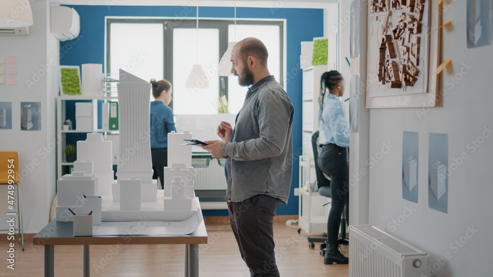 Architect using digital tablet and building model to design blueprints ...