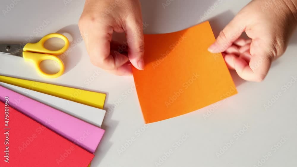 close-up of female hands fold colored paper, makes hearts using origami ...