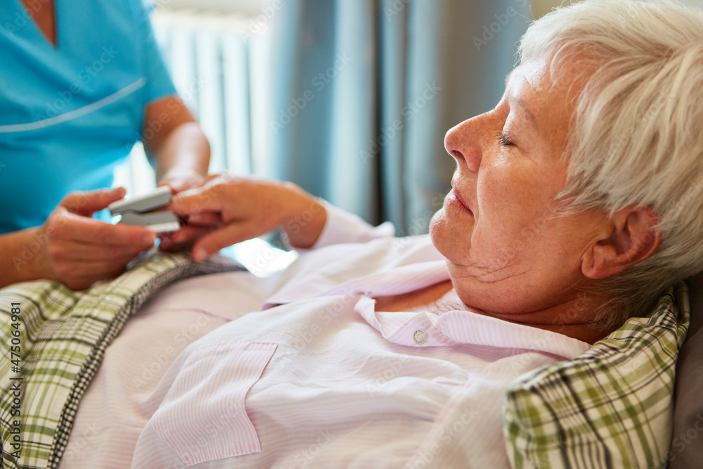 Geriatric nurse measures the pulse of a sick elderly woman in bed Stock ...