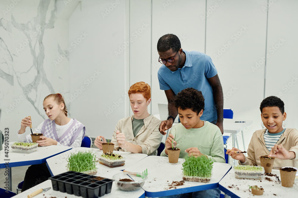 Diverse group of children planting seeds while experimenting at biology ...