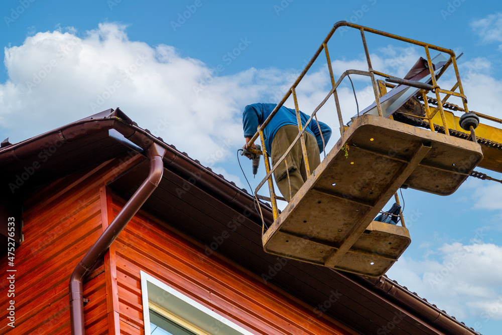 A work carpenter repairs the roof of a wooden house at a construction ...