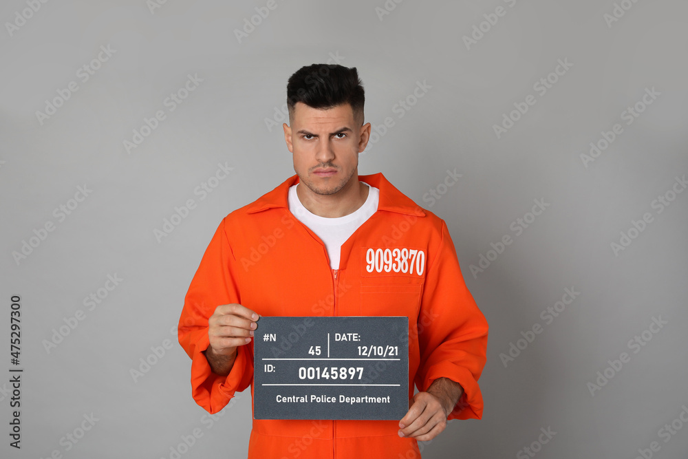 Mug shot of prisoner in orange jumpsuit with board on grey background ...