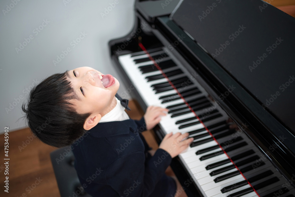 Asia boys wearing suit look up and smile or laugh playing grand piano ...