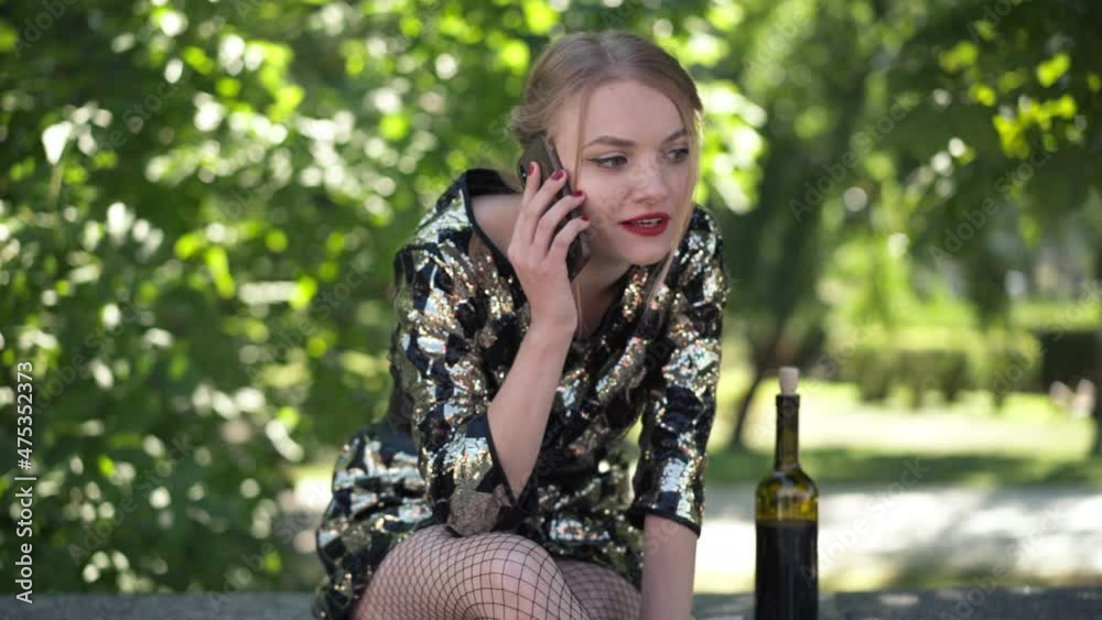 Young happy drunk woman sitting in city park talking on phone laughing ...