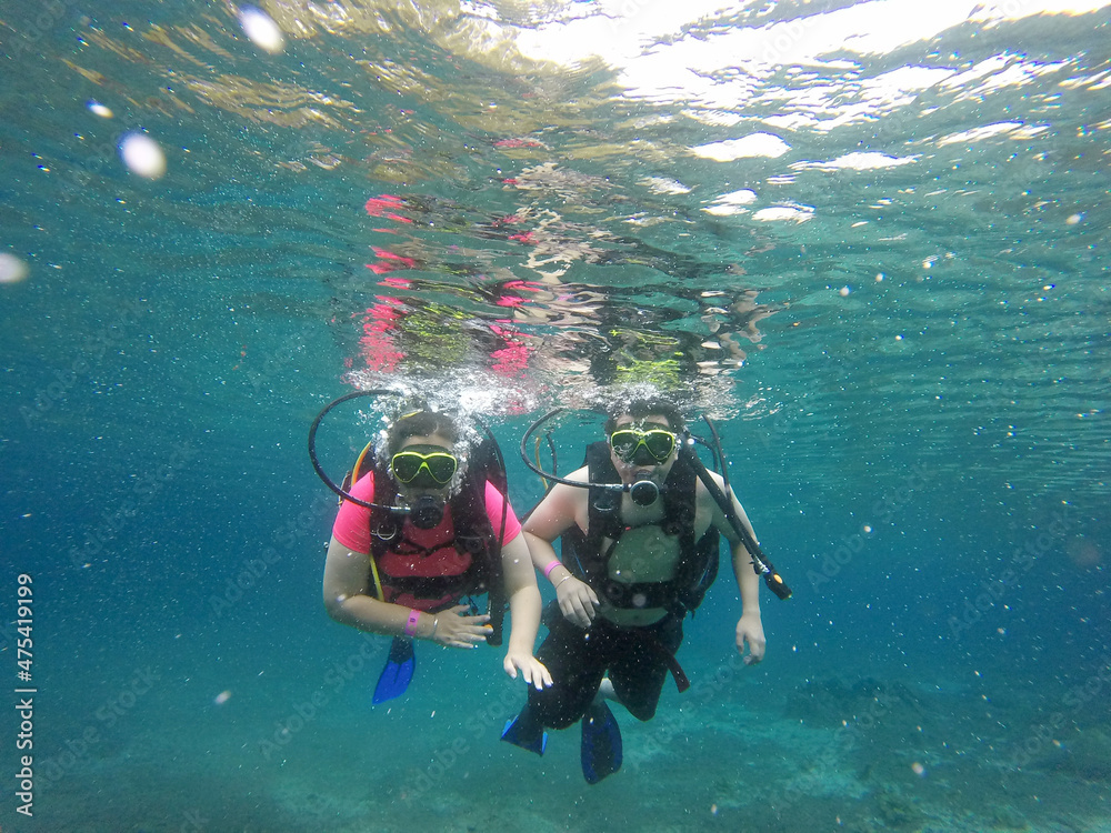 Couple scuba diving under crystal clear water with tank, fins and visor ...