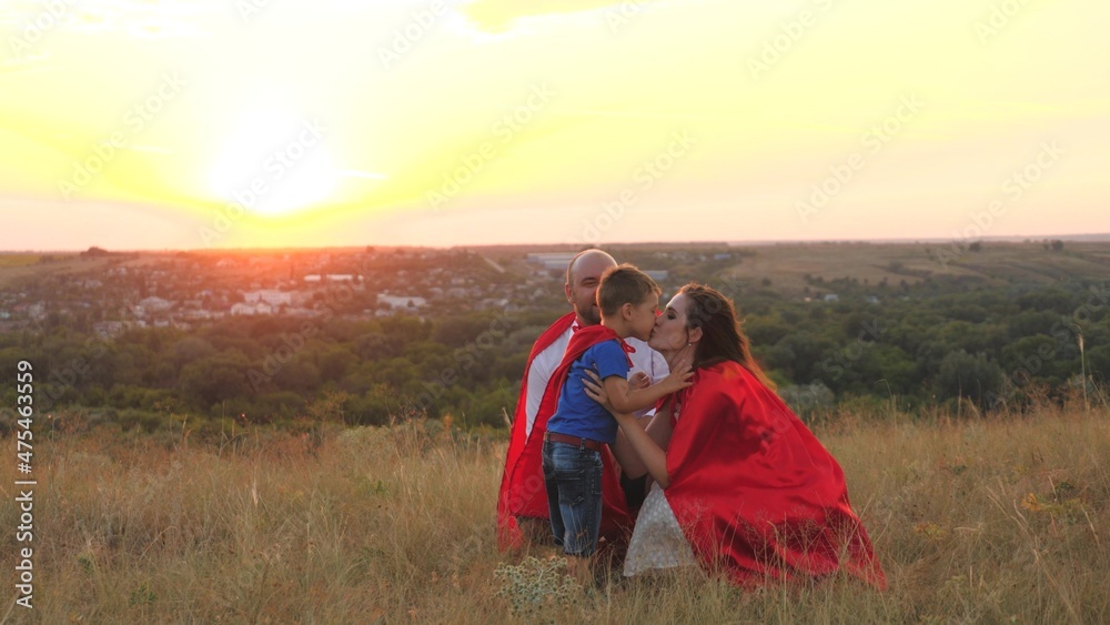 mother and father kiss and hug little child sunset, playing superheroes ...