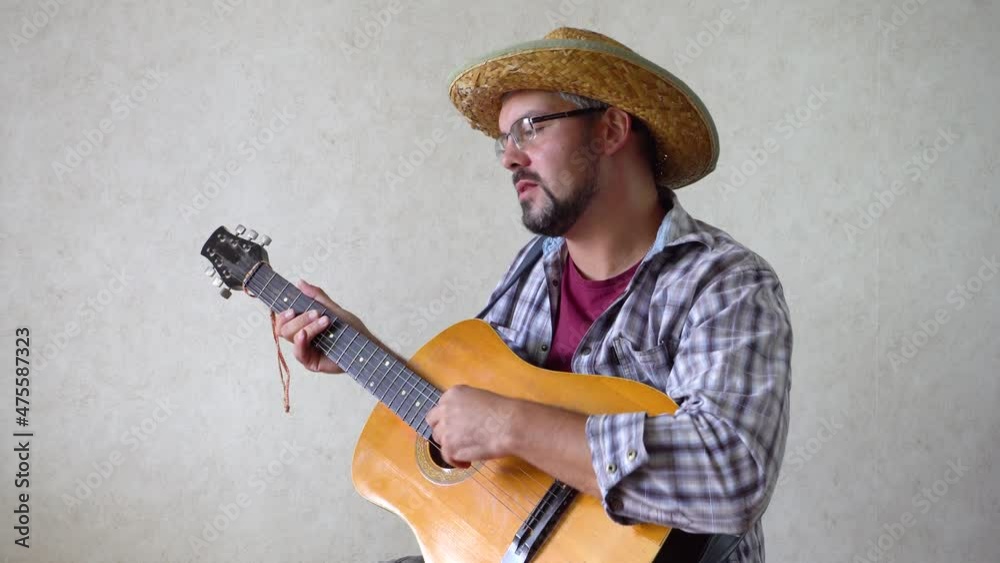 The man plays the guitar and sings. On his head is a straw hat ...