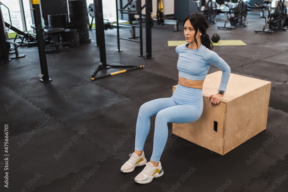 Pretty woman doing reverse push-up on triceps on crossfit box in gym ...