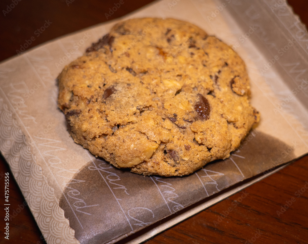 A big chocolate chip cookie placed on a butter paper packet. Wooden ...
