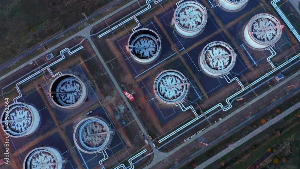 A top-down aerial view of rows of oil tanks connected by pipes at a ...