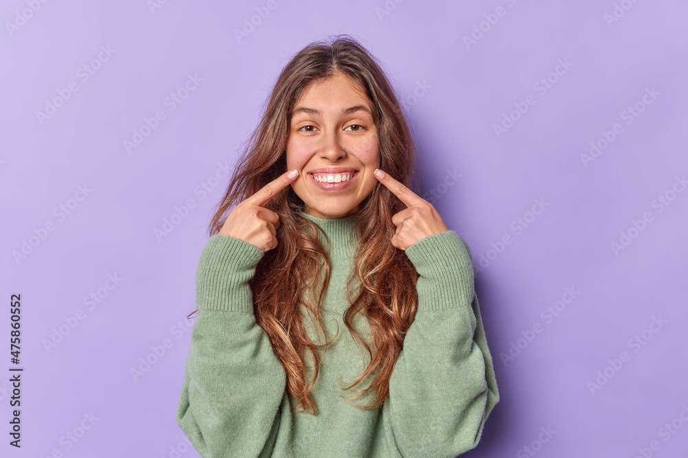 Young long haired brunette woman points index fingers at teeth and ...