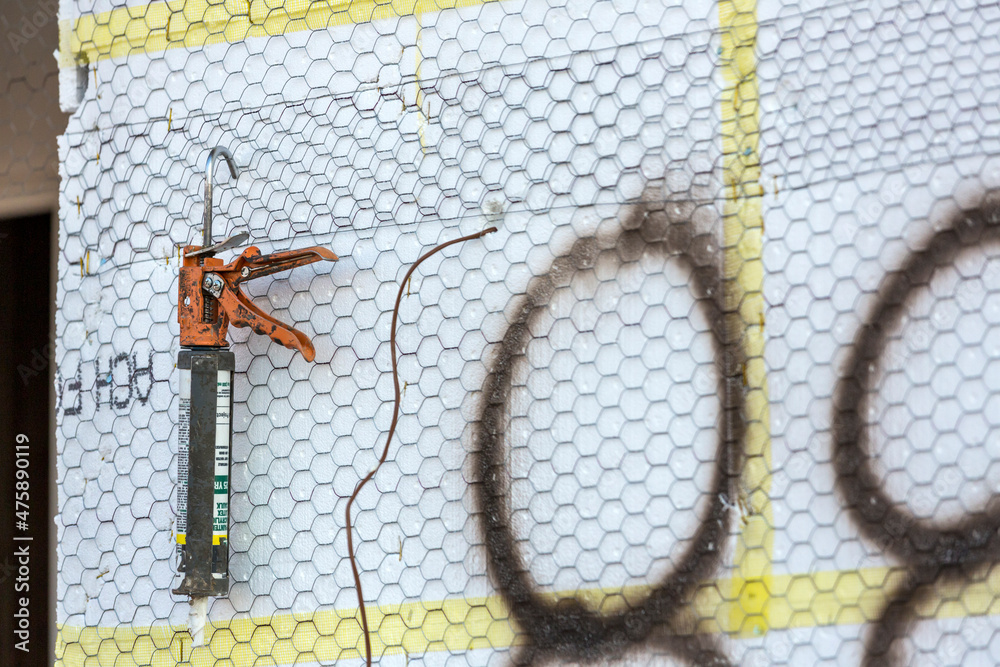 Caulk gun hanging on a wall covered in metal construction mesh near ...