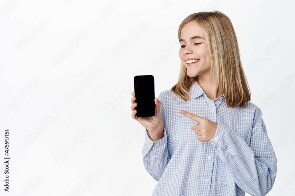 Cute blond girl, child pointing and showing on smartphone screen, empty ...