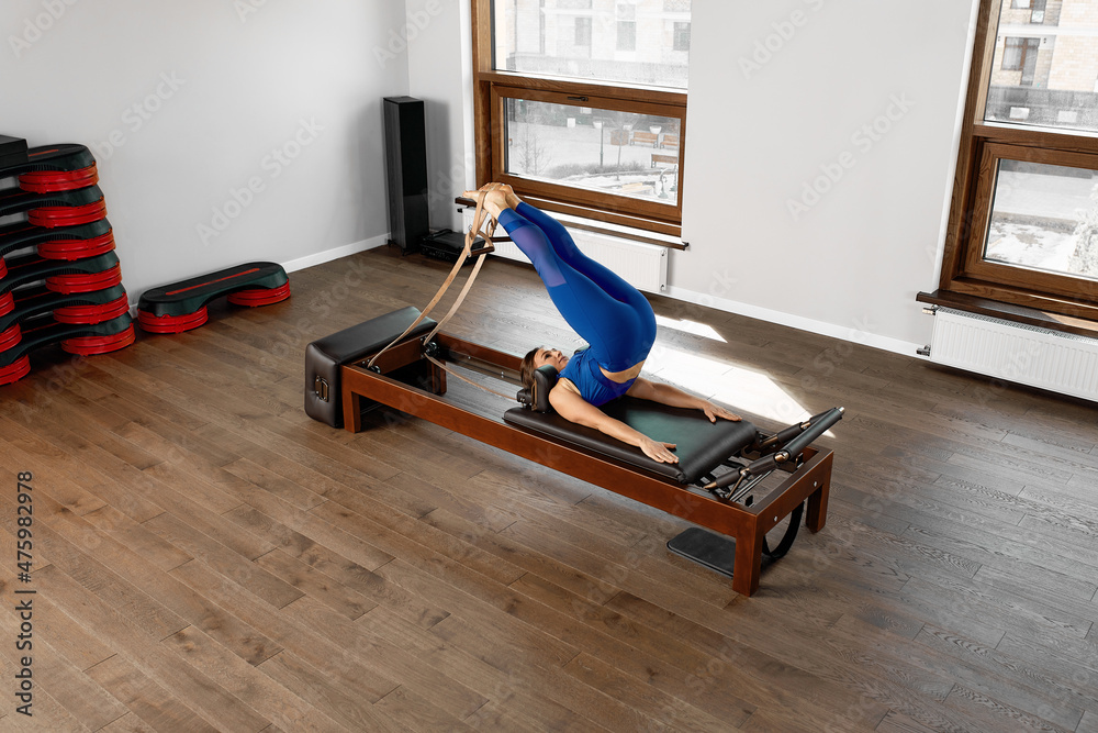 The instructor does exercises on the reformer, a beautiful girl trains ...