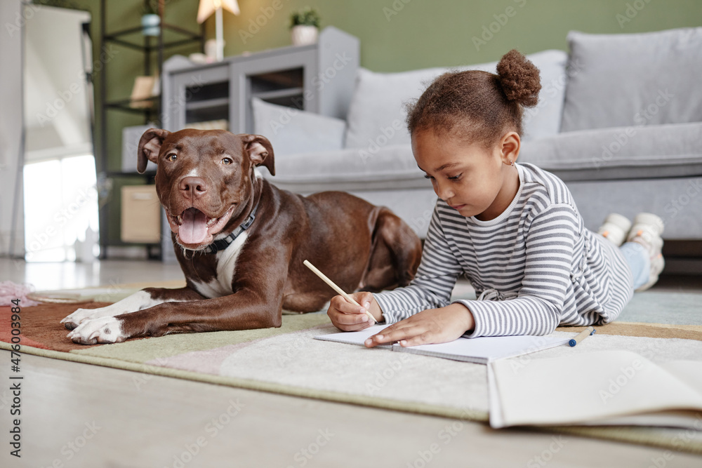 Full length portrait of cute African-American girl lying on floor with ...