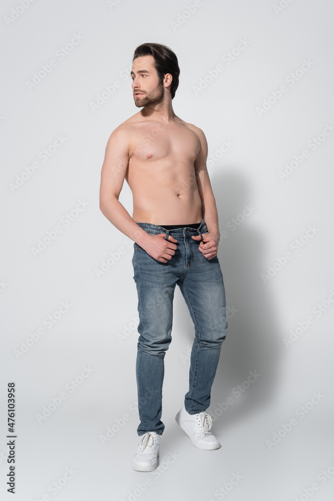 full length view of young shirtless man in jeans holding thumbs in belt ...