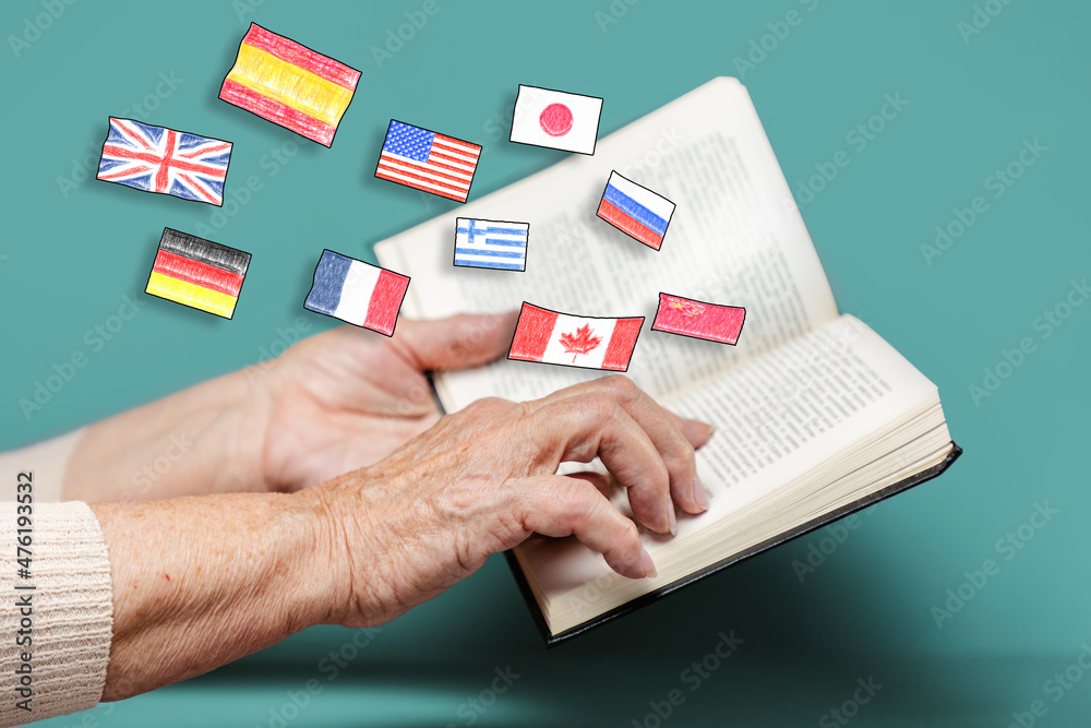 A senior woman reading a book with flags of different countries. Close ...