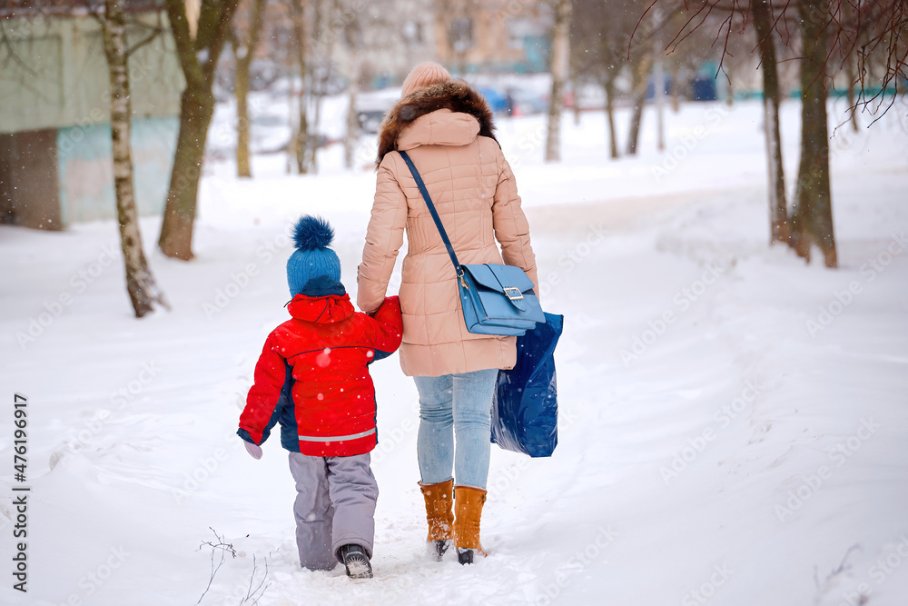 Mother and kid walks hard on unclean snowy path during snowstorm in ...
