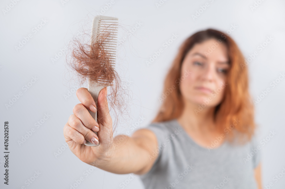 Caucasian woman with a grimace of horror holds a comb with a bun of ...