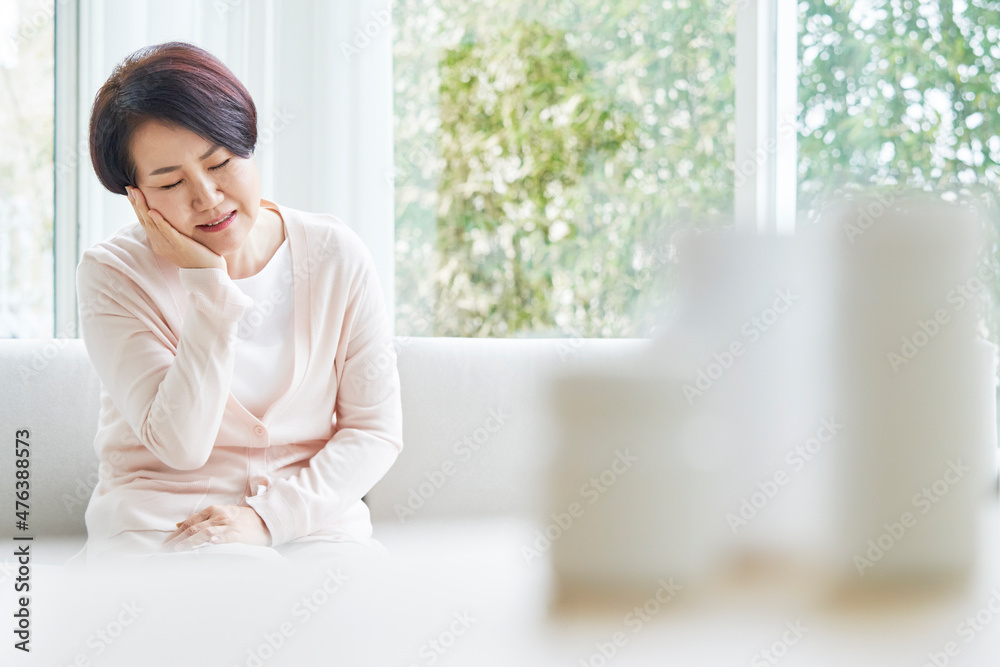Middle-aged woman suffering from stomatitis on the sofa in the living ...