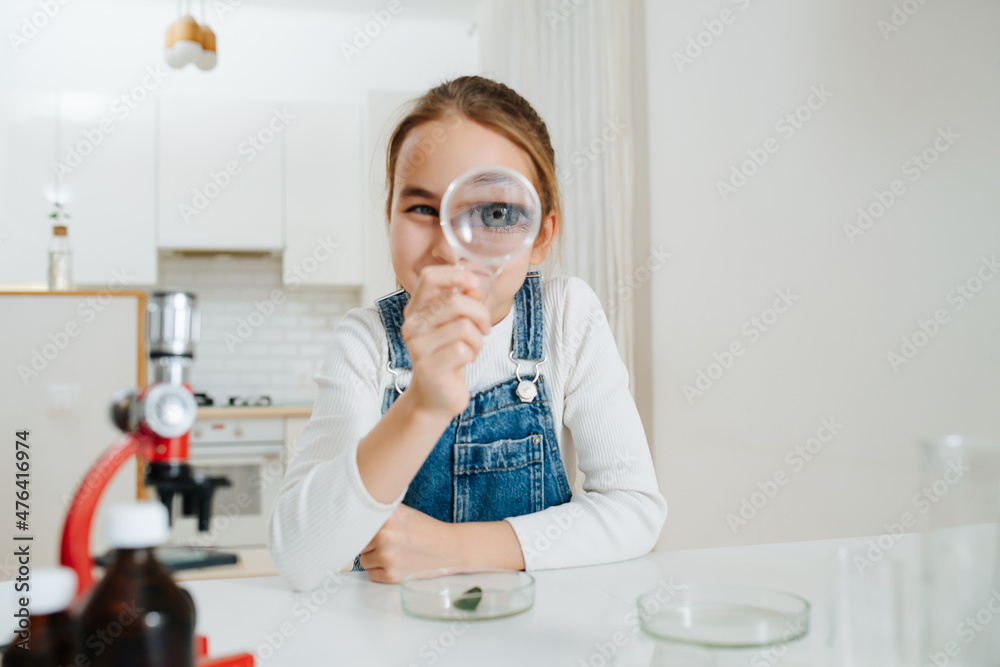 Silly little girl playing with magnifying glass while doing home ...