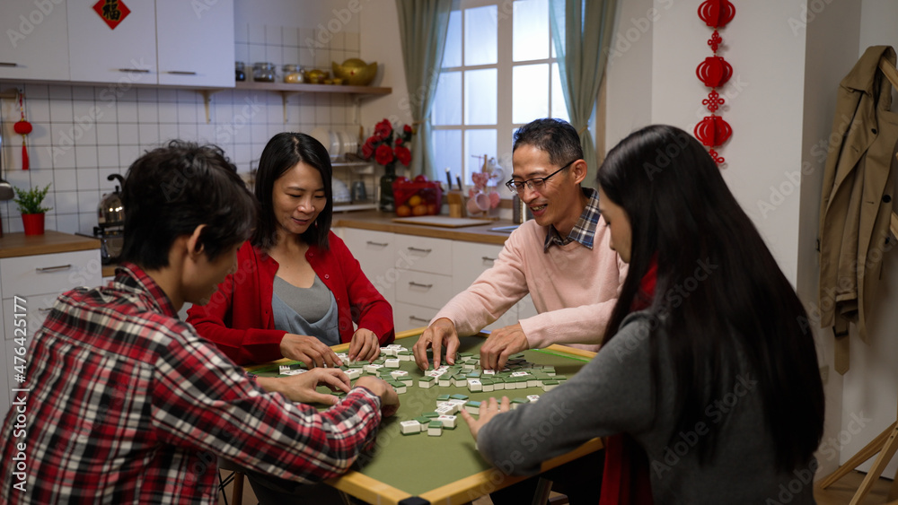 asian family of four shuffling tiles while playing mahjong together on ...