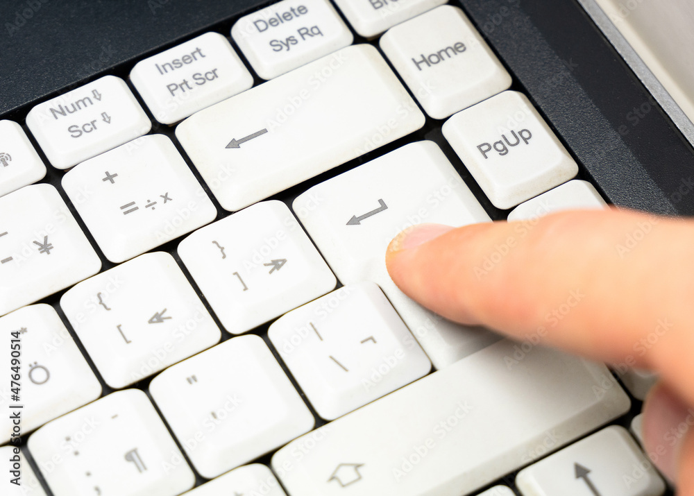 Man pressing the enter key on a simple plain white laptop keyboard ...