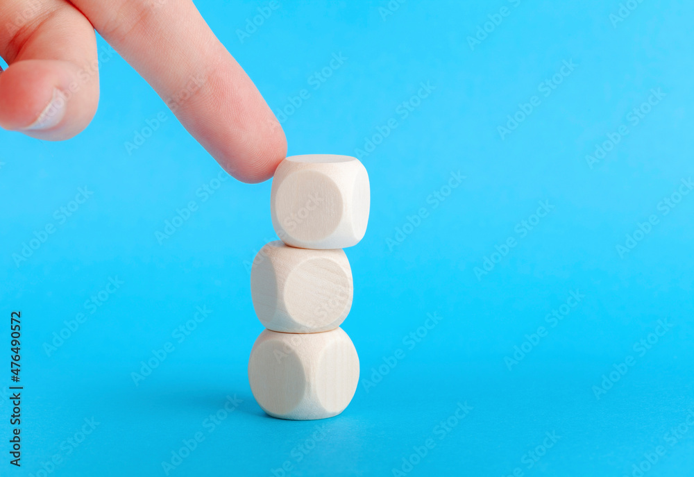 Finger knocking over a small tower of three blank wooden cubes, blocks ...