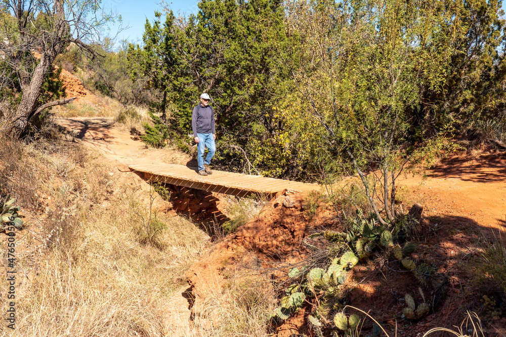 Mature Caucasian man walking across a dry stream on a wooden plank ...