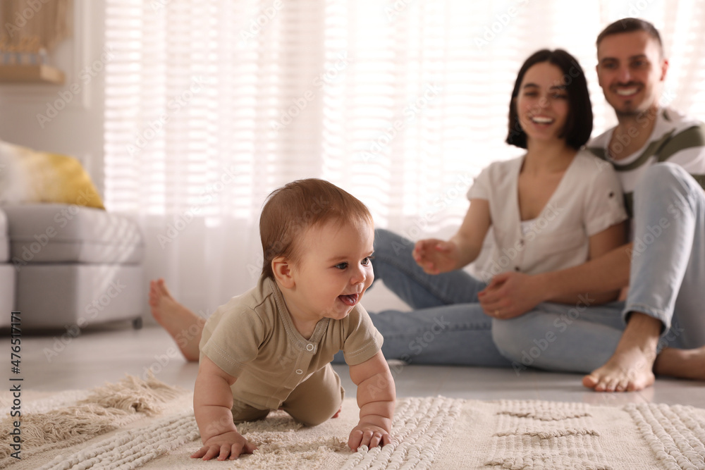 Happy parents watching their cute baby crawl on floor at home Stock ...