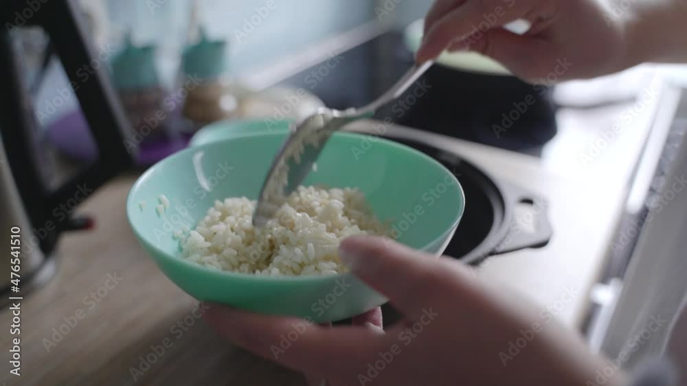 Woman puts fresh steamed white rice into deep blue plate with spoon ...