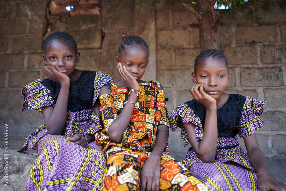 Three beautiful young welldressed black African girls sitting side by ...