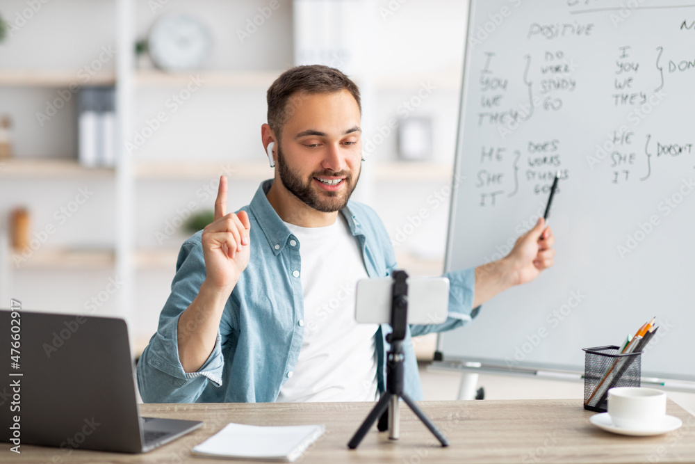 Young male teacher giving online English lesson, pointing at blackboard ...