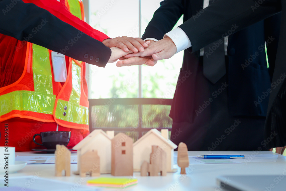 Business people and engineer putting hands together over meeting desk ...