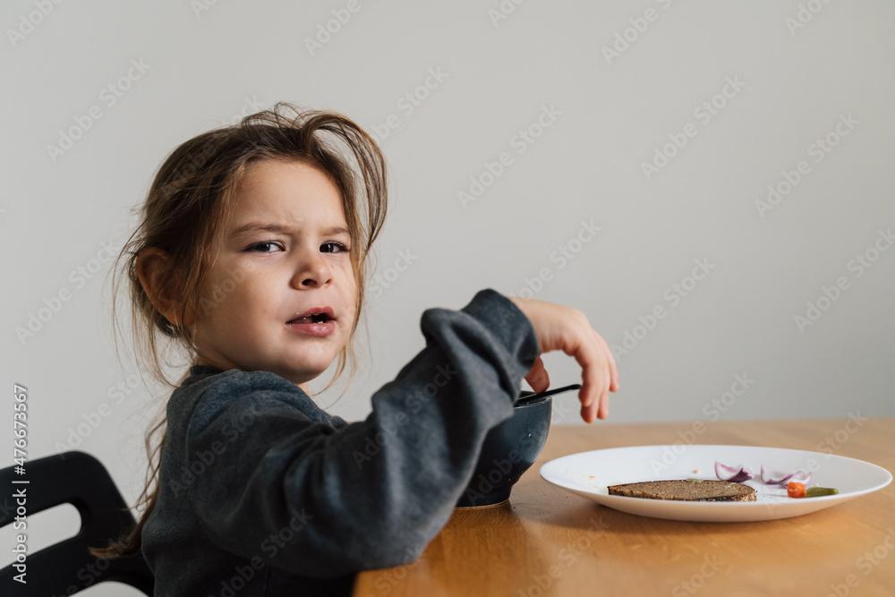 Unhappy child girl eats soup from black bowl with bread and onion ...