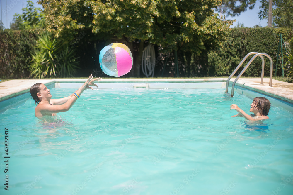 Joyful brothers playing ball in swimming pool. Two schoolboys with long ...
