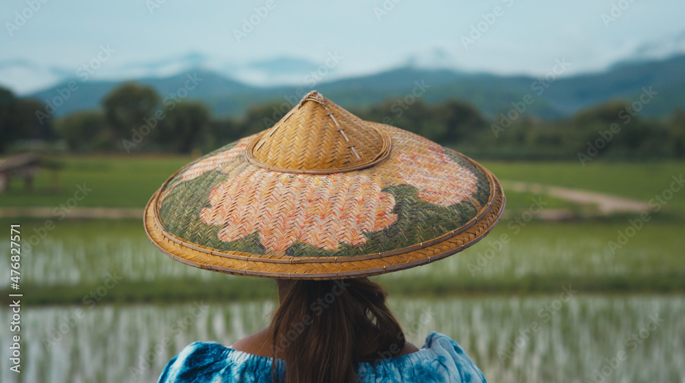 Woman rom behind wearing straw hat with rice fields and foggy mountains ...