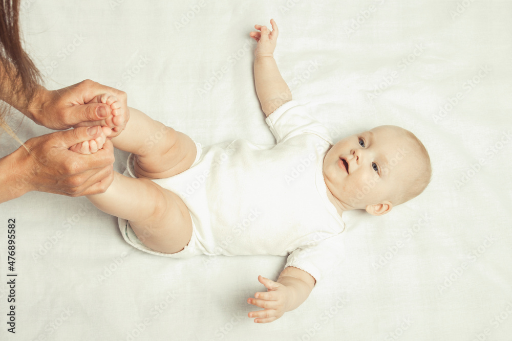 Mom does gymnastics to a little baby on the bed with a white sheet. The ...