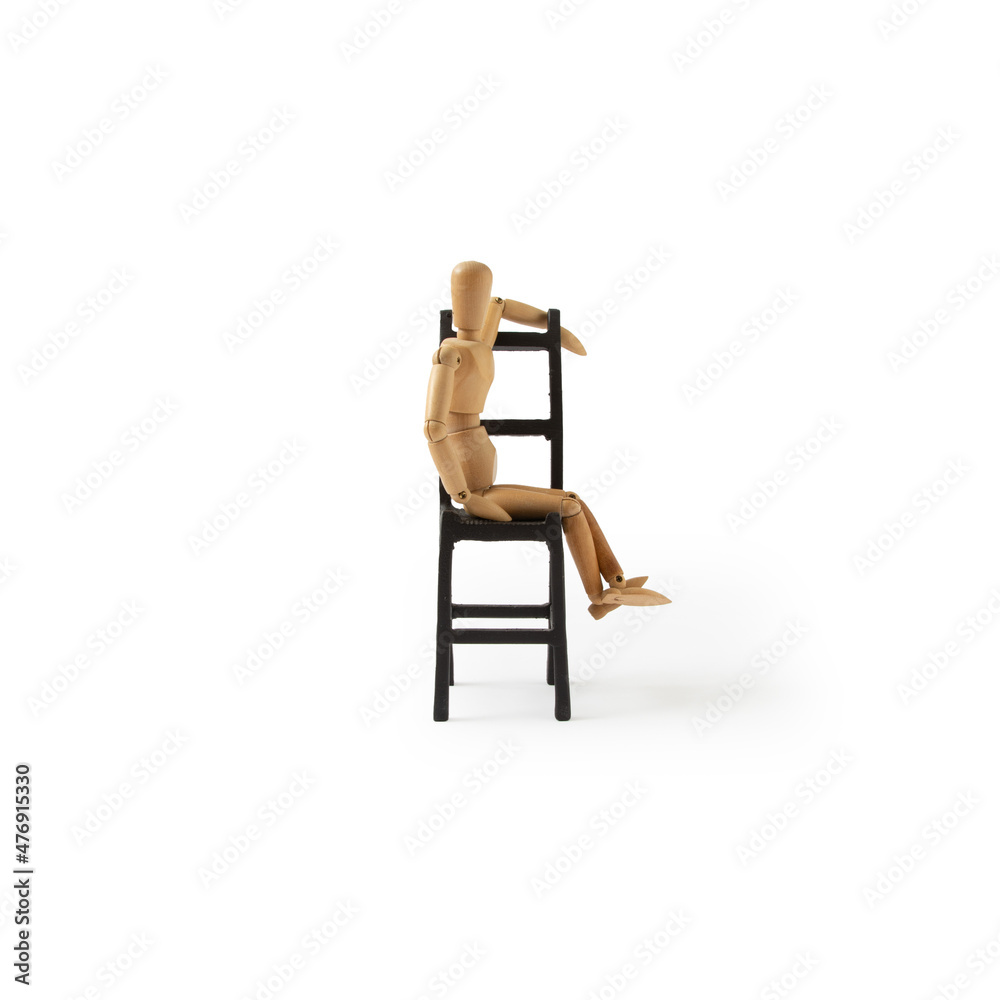 A wooden mannequin sits on a black chair on a white background. A ...