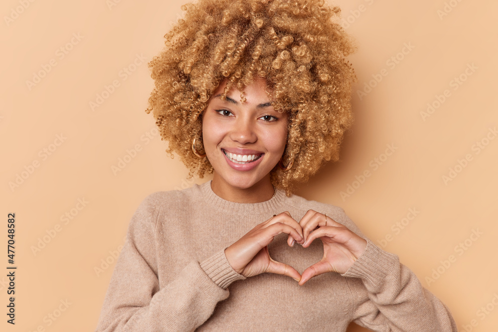 Romance concept. Positive curly haired young pretty woman makes heart ...