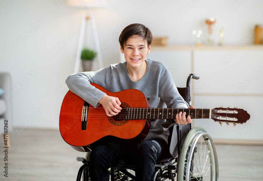 Happy disabled teen boy in wheelchair playing guitar, using musical ...