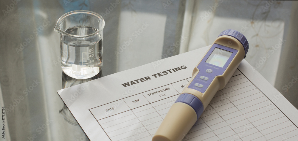 Portable pH meter and water testing sheet on the table. Becker with ...