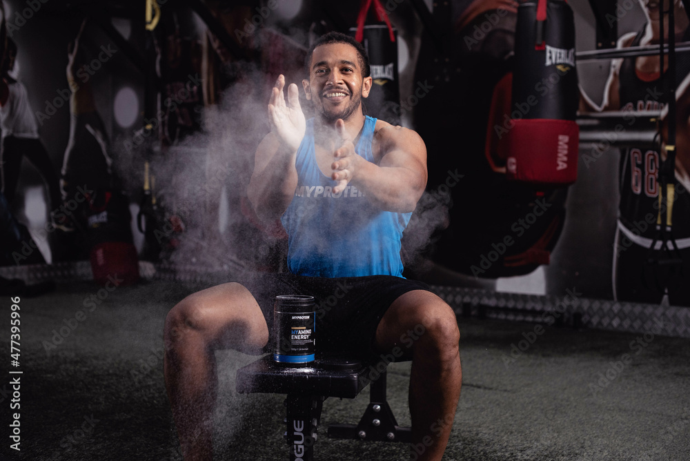 Smiling man spreading powder from protein container sitting on a stool ...