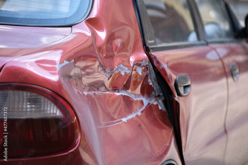 Dented car with damaged body parked on city street side. Road safety ...