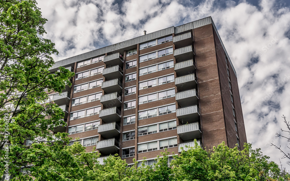 The corner of a 70s era apartment building is framed by green trees ...