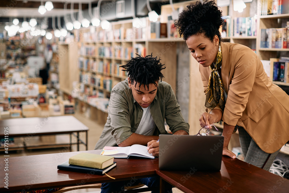 African American student e-learns with help of his teacher in library ...