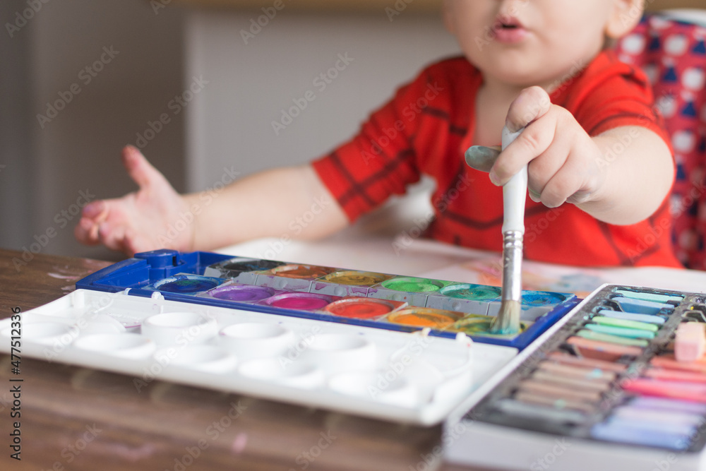 18 month old toddler makes excited expression while dipping paint brush ...