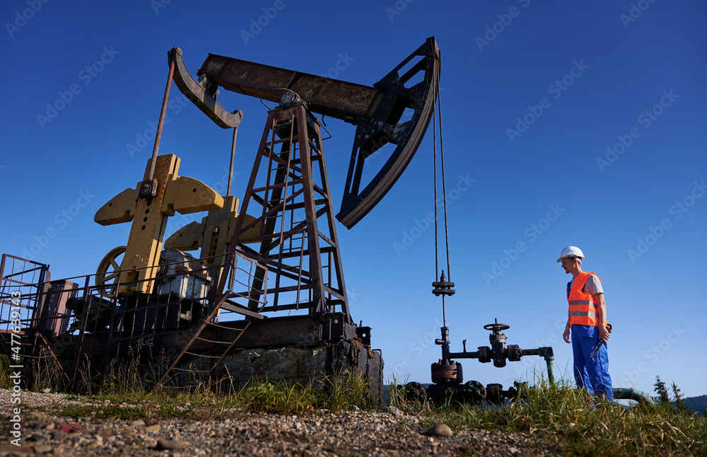 Against cloudless sky operator standing near oil pipeline with spanner ...