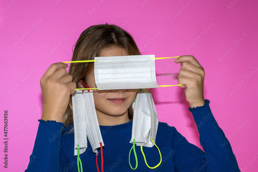 A teenage girl holds a medical disposable mask in her hands, several ...