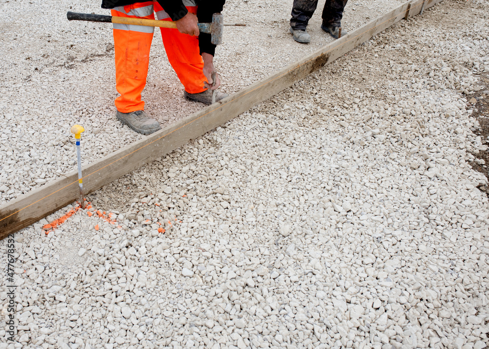 Groundworker in orange safety hi vis trousers fixing a timber along ...